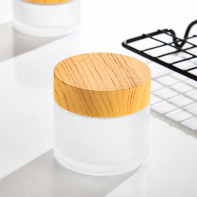 木製のふたは透明なガラス化粧品のクリーム色の容器を曇らした